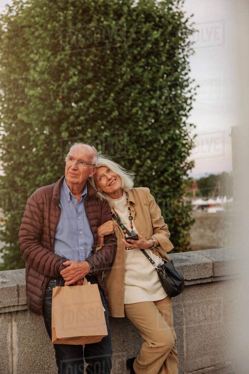 Thoughtful senior couple leaning on railing while looking away ...