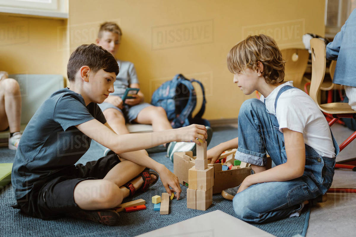 Male and female students stacking blocks while sitting on floor in ...