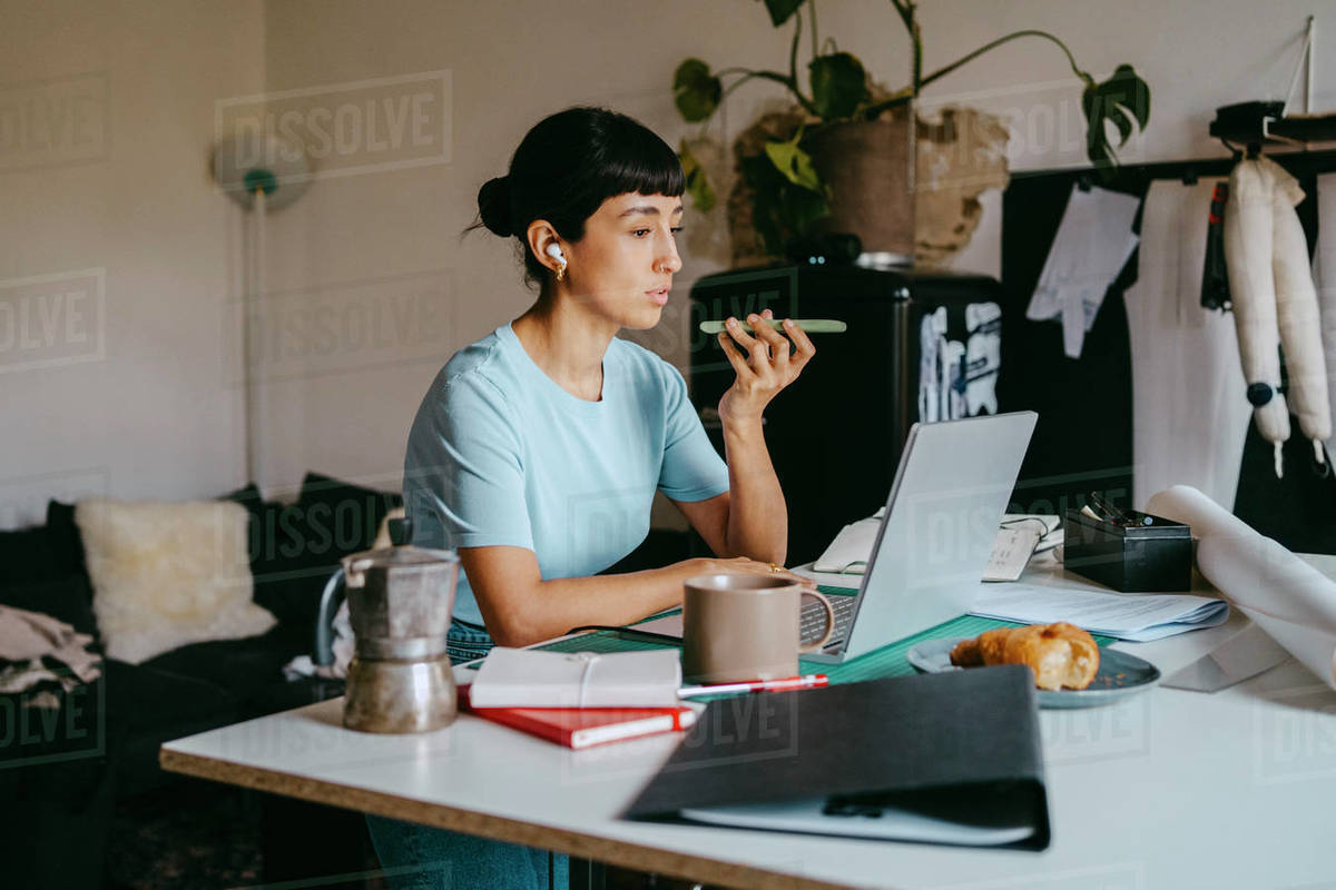 Female business professional talking on speaker phone and using laptop ...