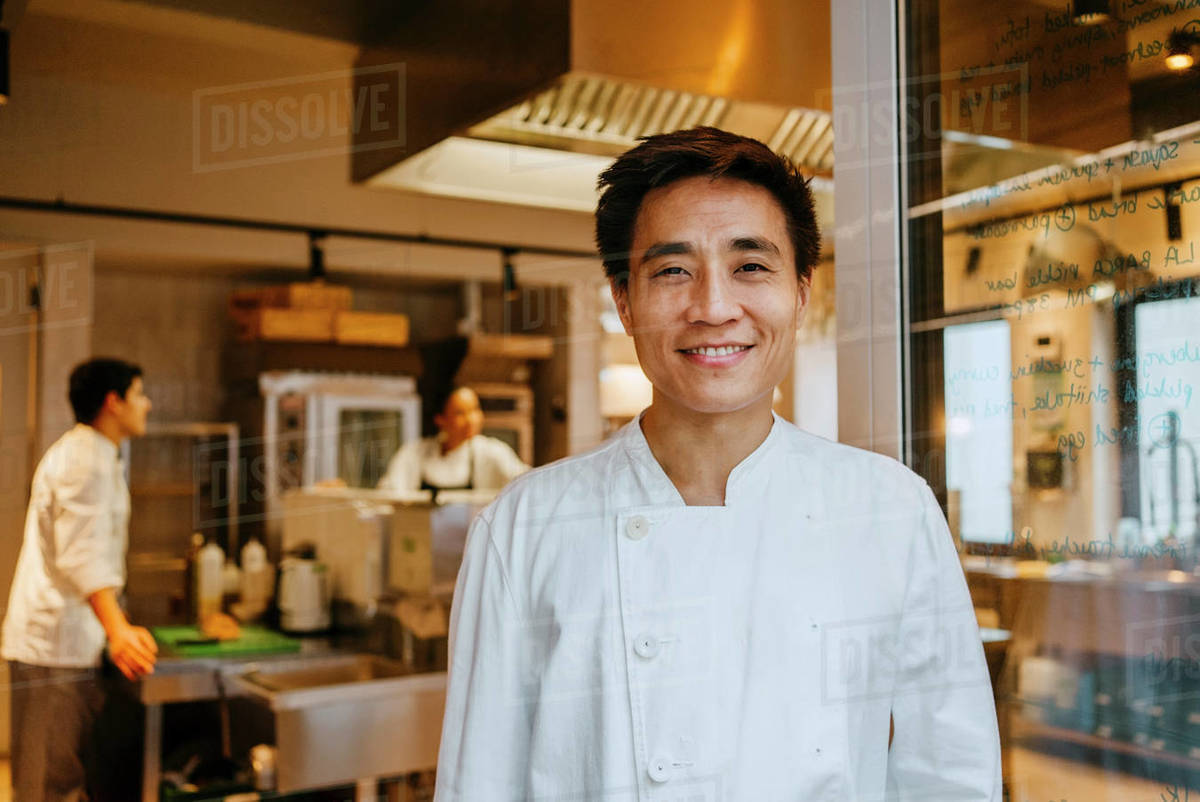 Portrait of happy male chef standing at door in commercial kitchen ...