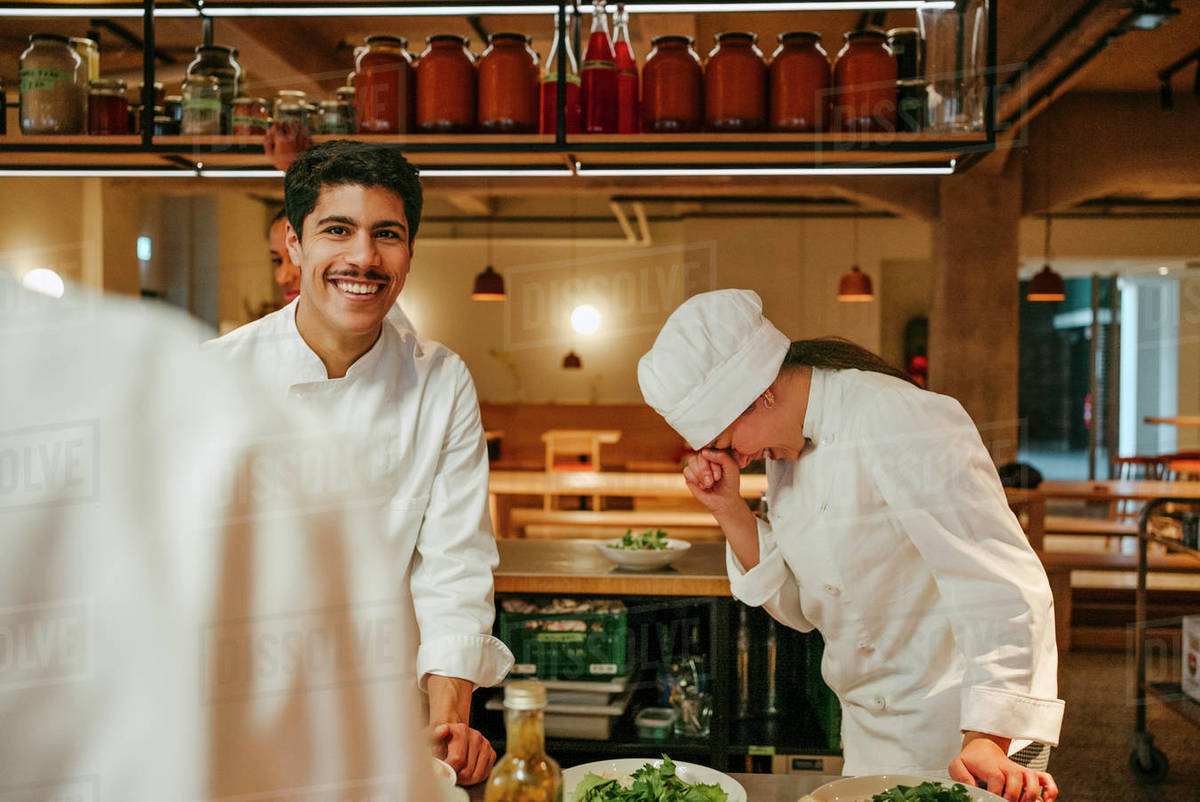 Male and female chef laughing with coworkers while working in ...