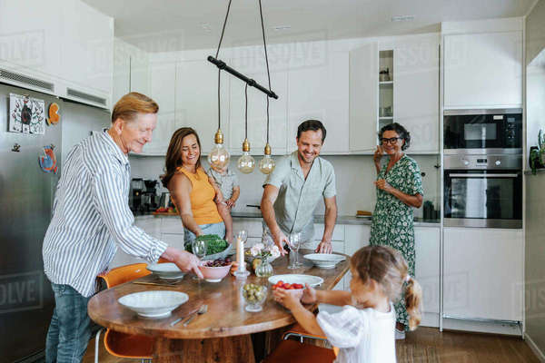 Happy multi-generational family helping each other in setting dining ...