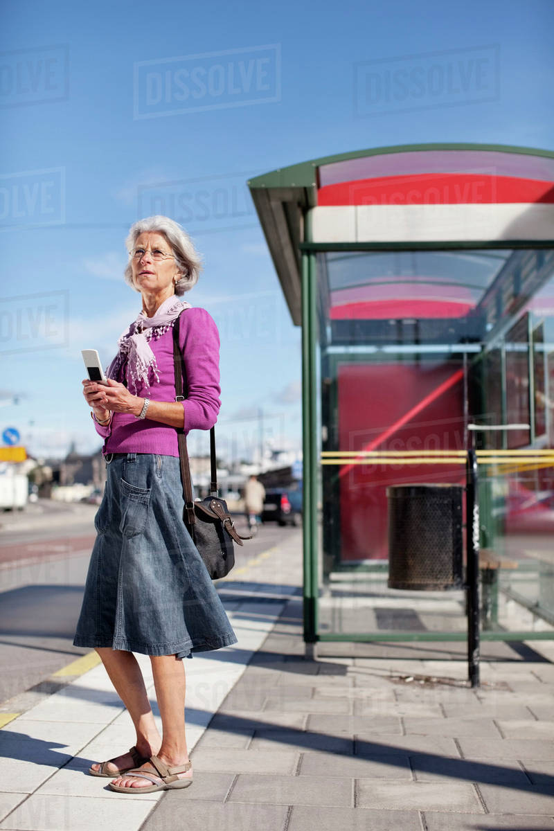 Senior woman standing at bus stop waiting - Royalty-free Stock Photo ...