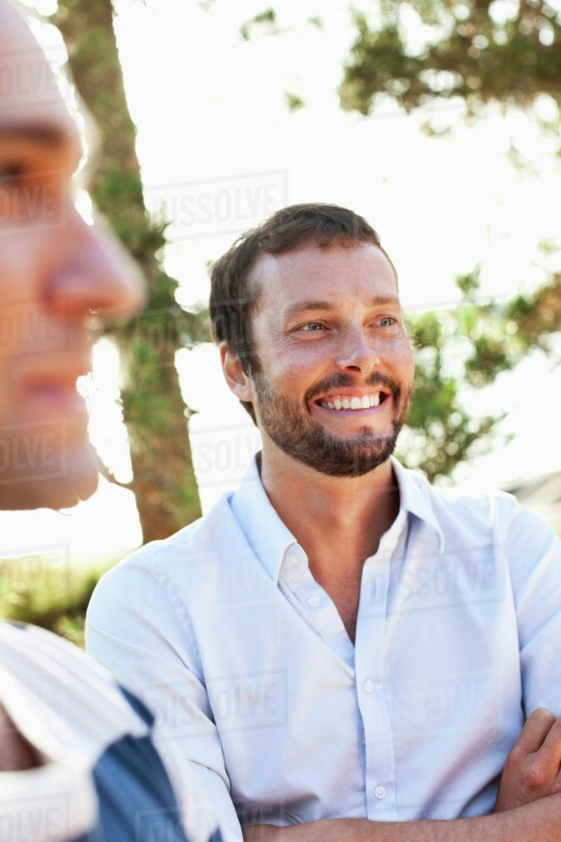Man smiling while sitting with friends - Stock Photo - Dissolve