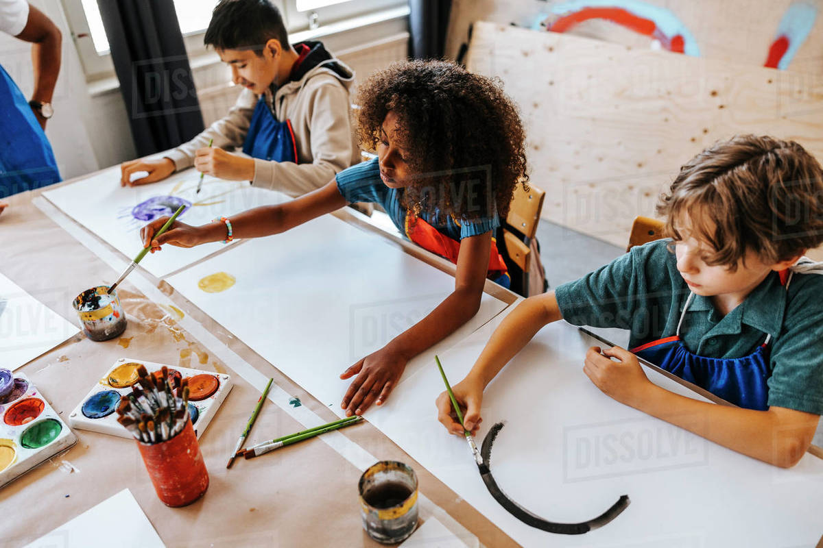 High angle view of male and female students painting on paper in art ...