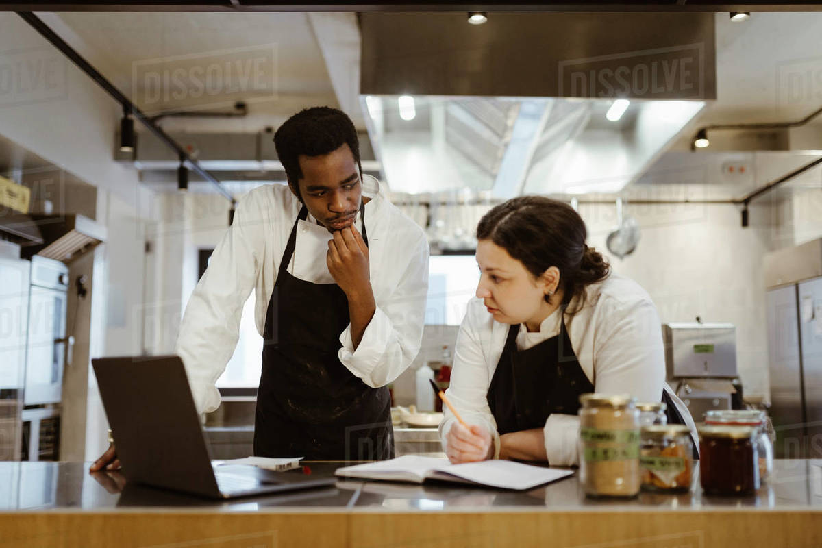 Female chef leaning on counter while discussing with male colleague in ...