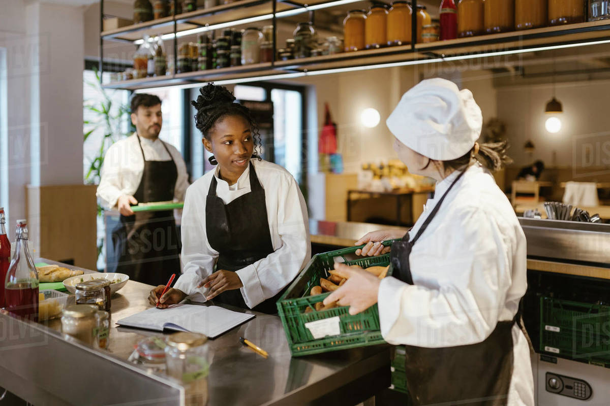 Female chef holding crate and taking inventory with colleague in ...