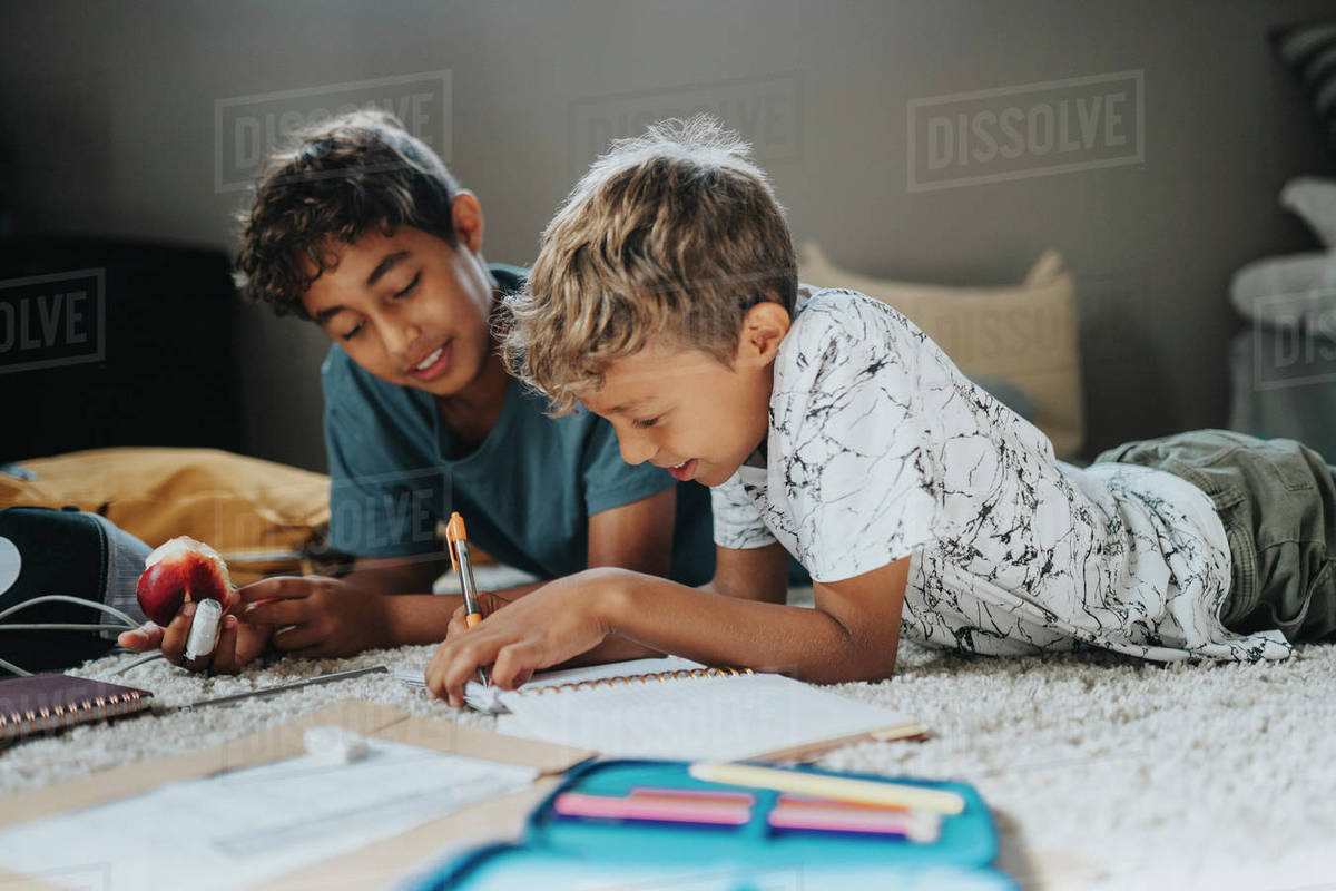 Multiracial boys doing homework while lying on front at home - Royalty ...