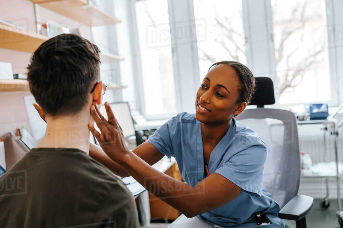 Smiling female medical professional checking lymph nodes of patient in ...