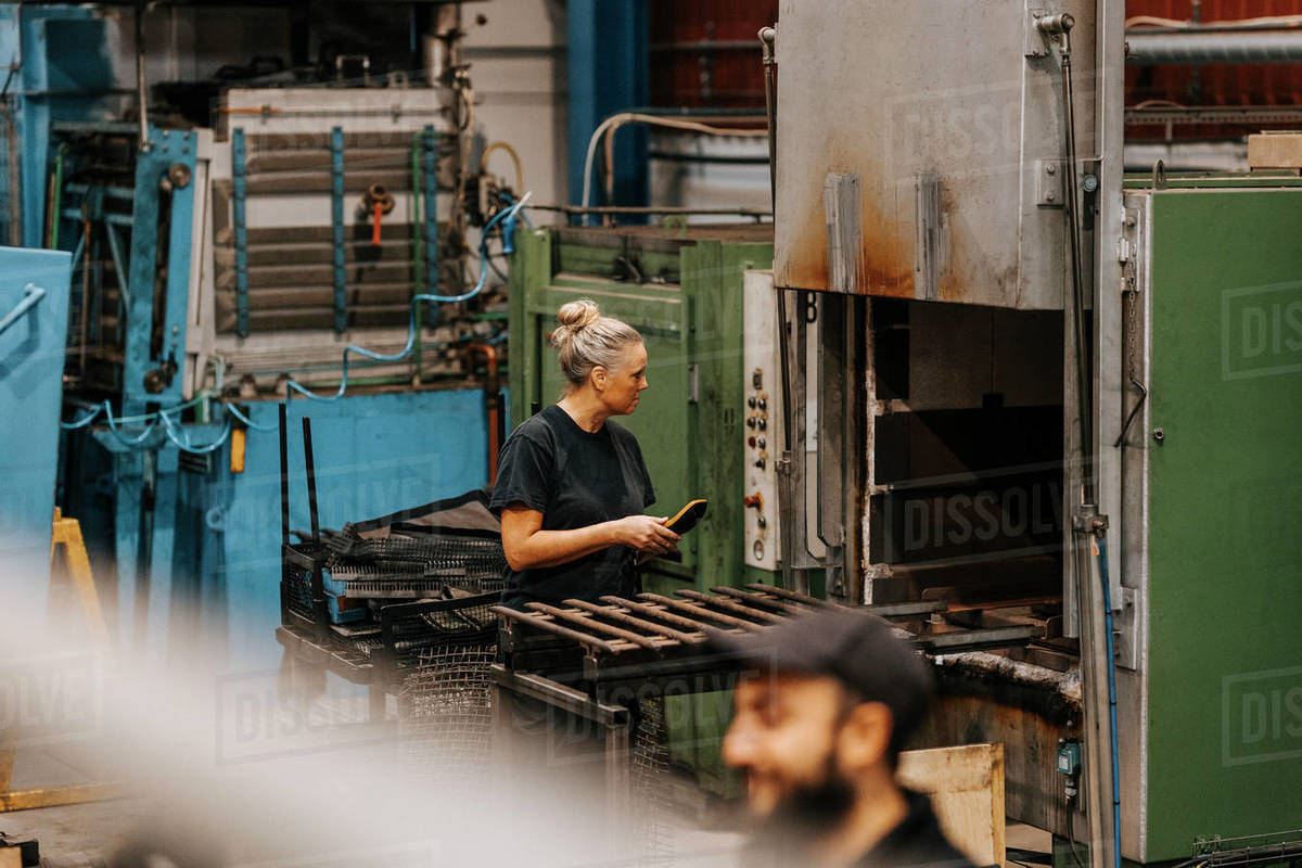 Focused mature female factory worker operating machine while working ...
