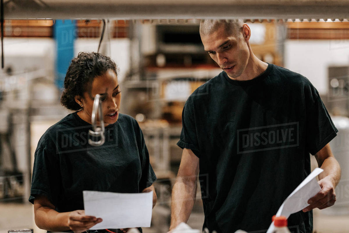 Front view of multiracial male and female factory workers discussing ...