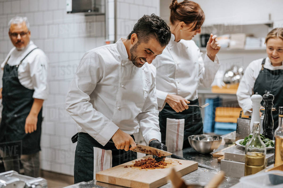 Happy male chef chopping food on cutting board while working with ...