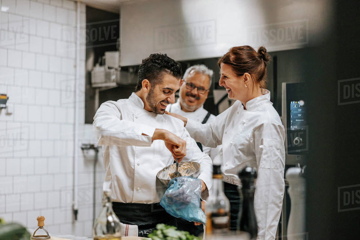 Happy female chef with hand on shoulder of male colleague putting ...