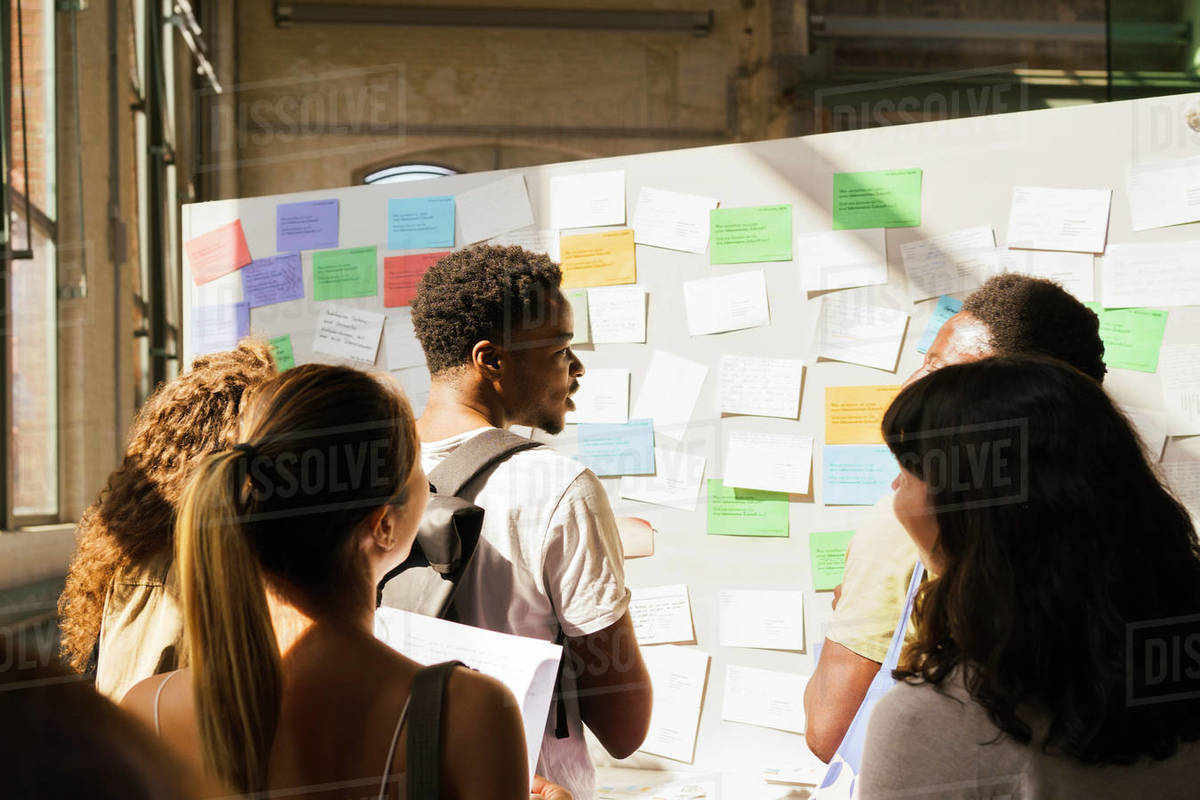 Multiracial male and female students searching on bulletin board in ...