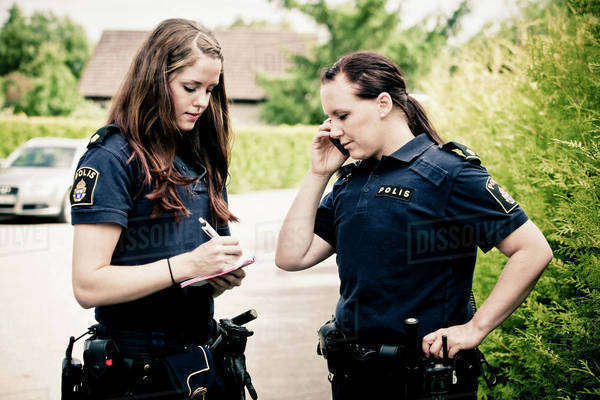Female police officer using cell phone while colleague writing notes ...