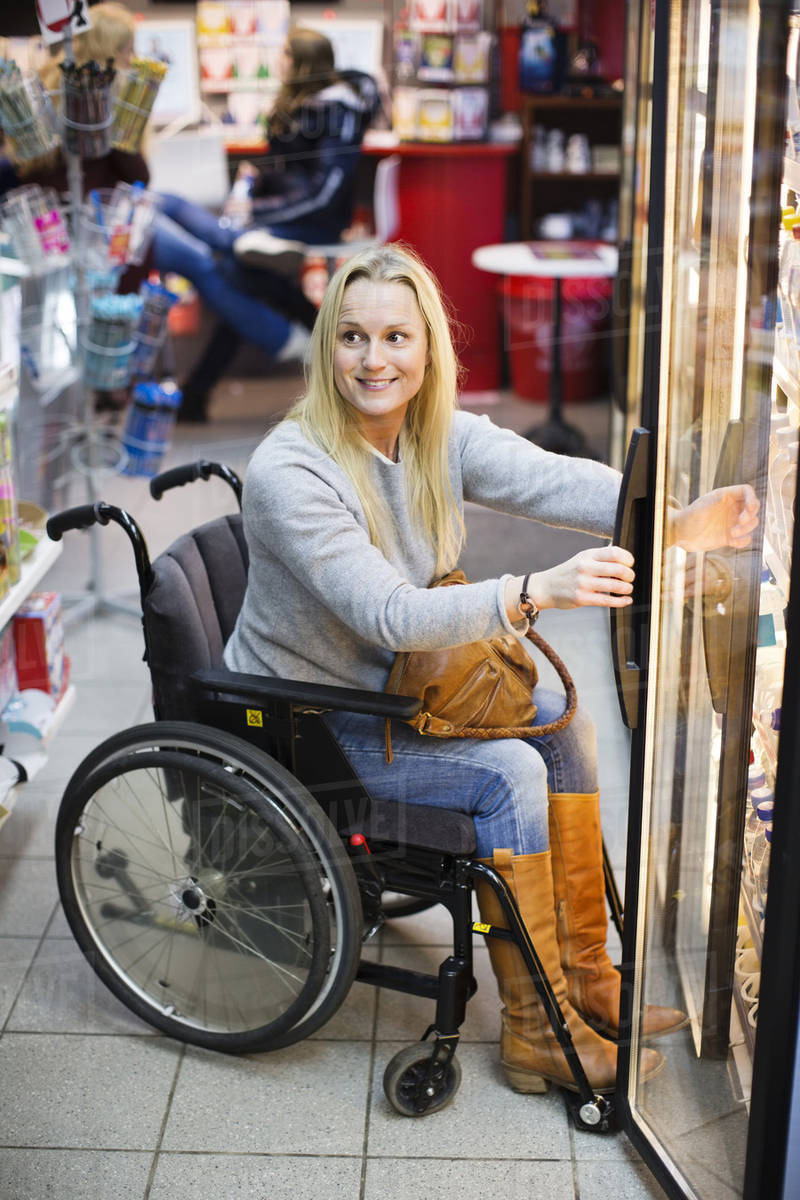 Happy disabled woman in wheelchair at refrigerated section of ...