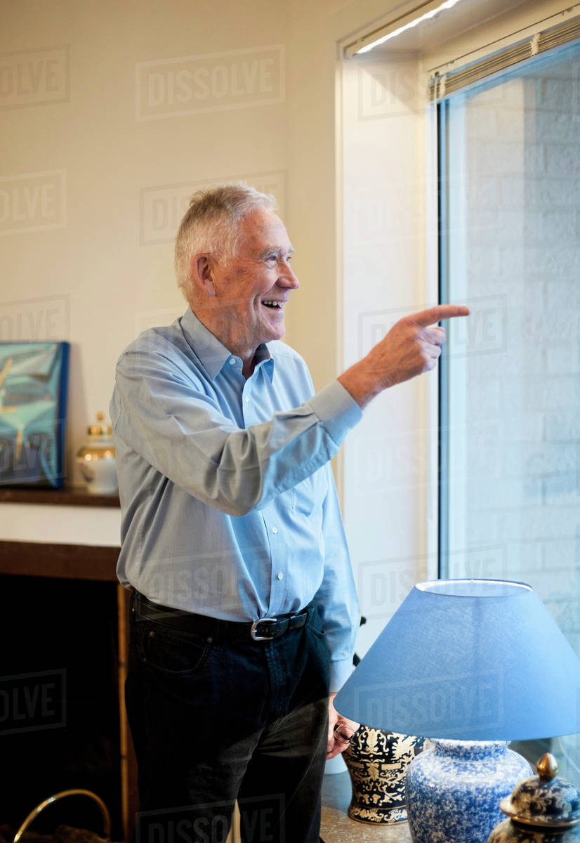 Happy senior man pointing at window - Stock Photo - Dissolve