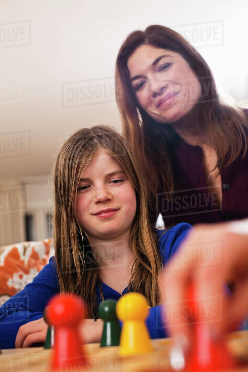 Mother watching daughters playing ludo at table - Stock Photo - Dissolve