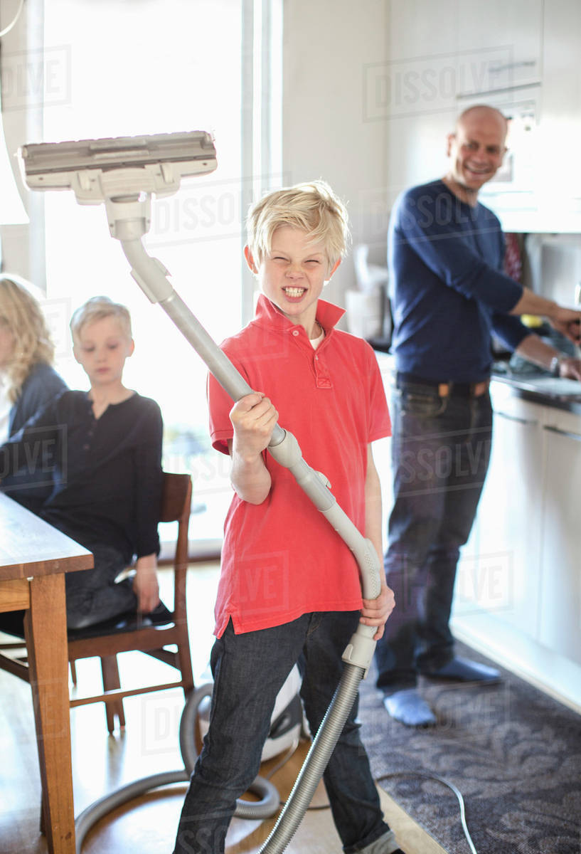 Portrait of boy clenching teeth while holding vacuum cleaner at home ...