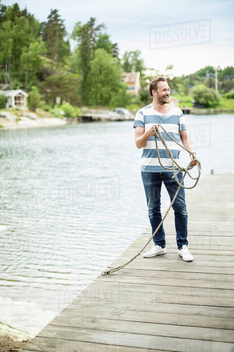 Happy man holding rope while standing on pier - Royalty-free Stock ...