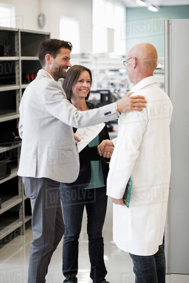 Smiling business people greeting engineer in manufacturing plant ...