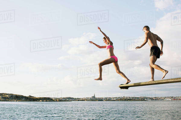 Full length of young couple diving into lake against cloudy sky - Stock ...