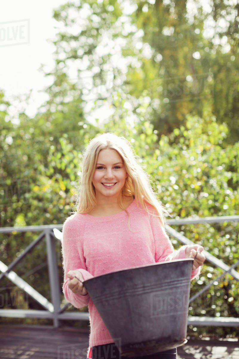 Portrait of smiling teenage girl carrying container in yard - Stock ...