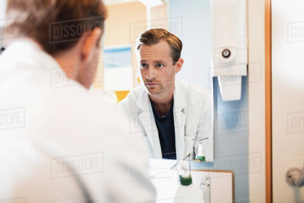 Mirror reflection of mid adult male doctor in hospital bathroom ...