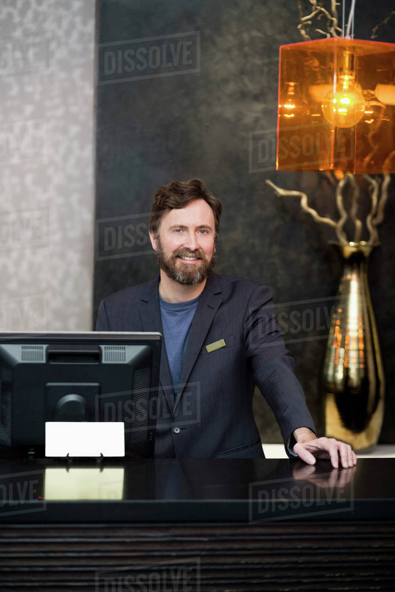 Portrait of smiling male receptionist standing at counter in hotel ...