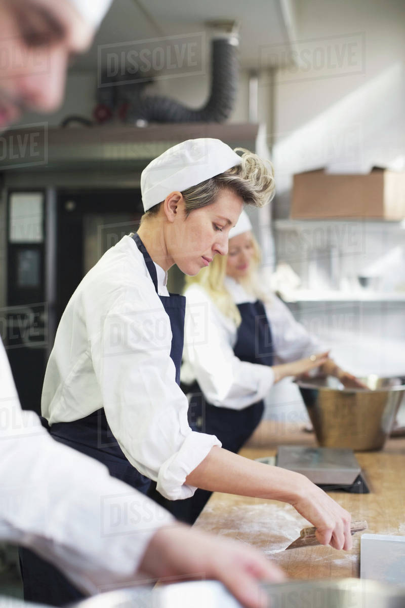 Side view of female baker baking with colleagues in commercial kitchen ...