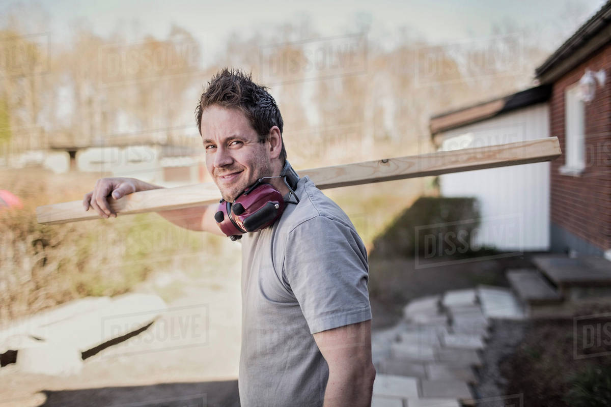 Side view portrait of smiling carpenter carrying wooden plank at ...