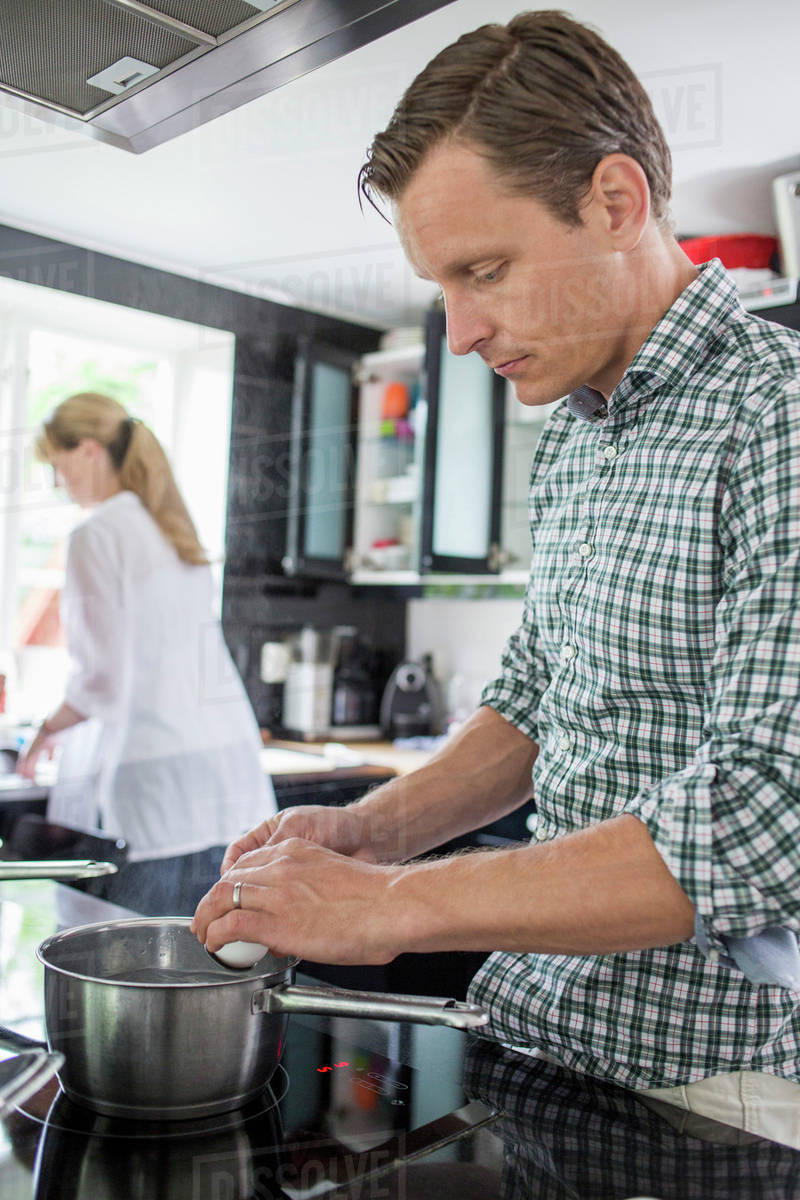 Husband cooking while wife cleaning utensils in background at kitchen ...