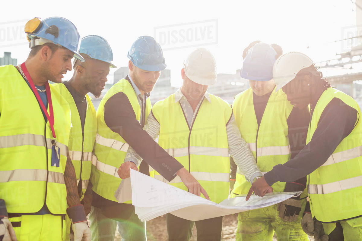 Architect explaining plan on blueprint to construction workers at site ...