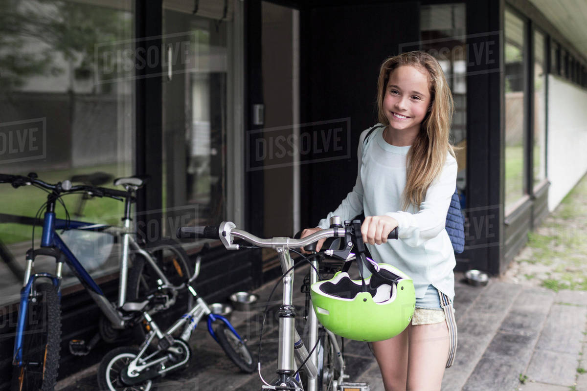 Happy girl walking with bicycle outside house - Stock Photo - Dissolve
