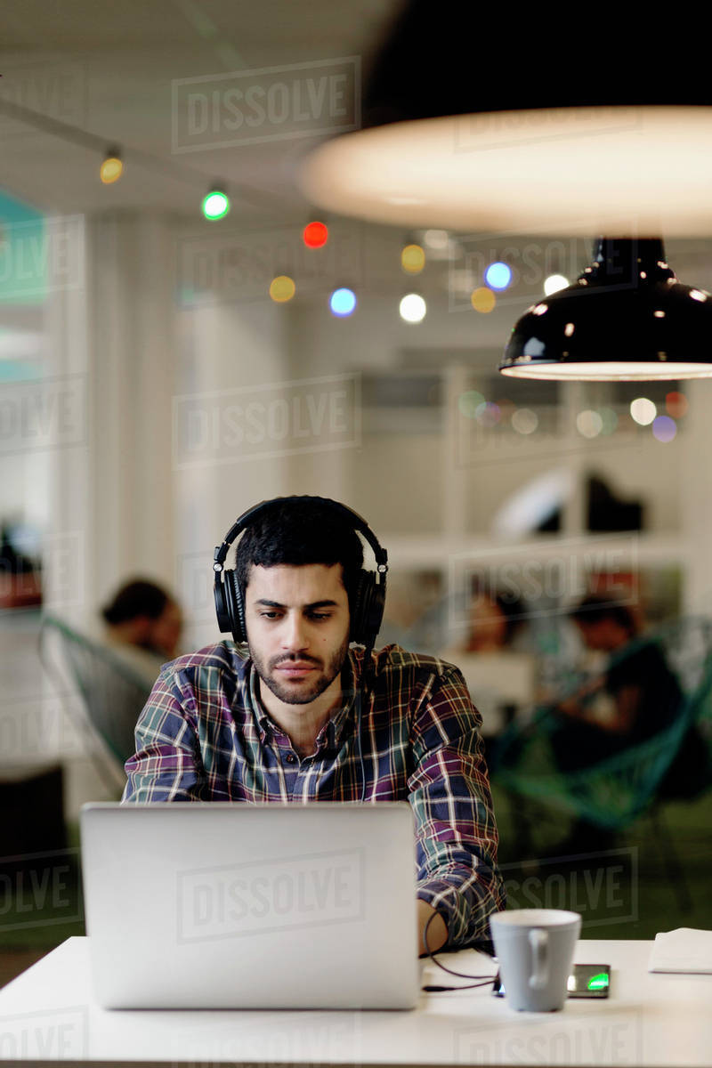 Businessman listening music while working late on laptop in creative ...