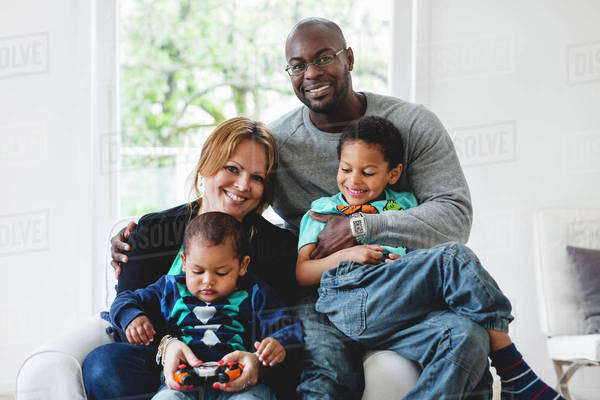 Portrait of happy multi-ethnic parents sitting with children at home ...