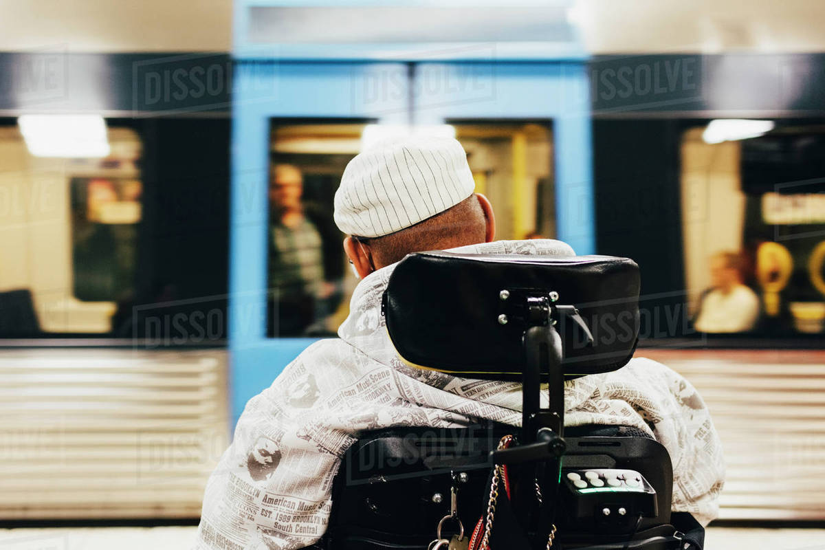 Rear view of man sitting in wheelchair against train at station ...