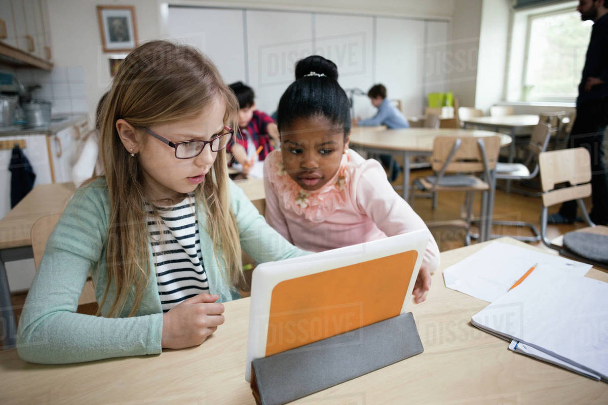 Serious students looking at digital tablet while sitting in classroom ...