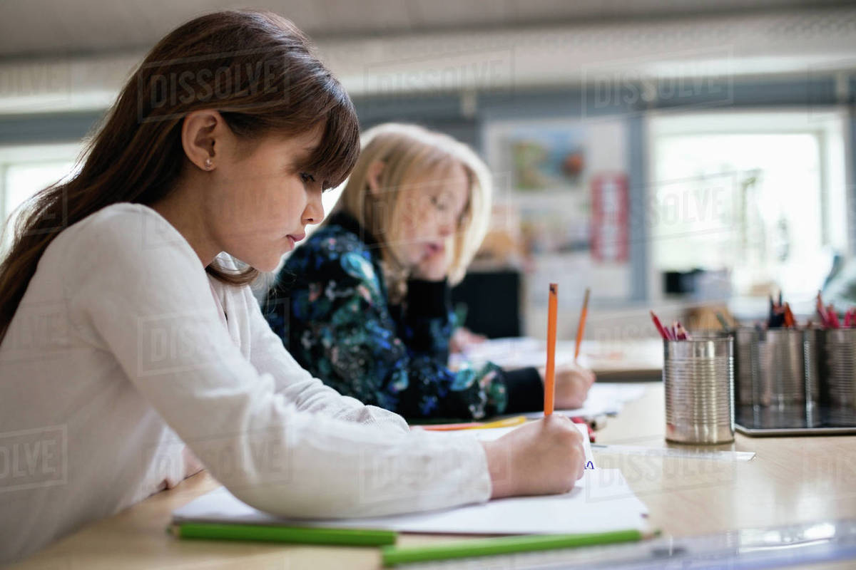 Side view of students writing on paper at desk in classroom - Royalty ...
