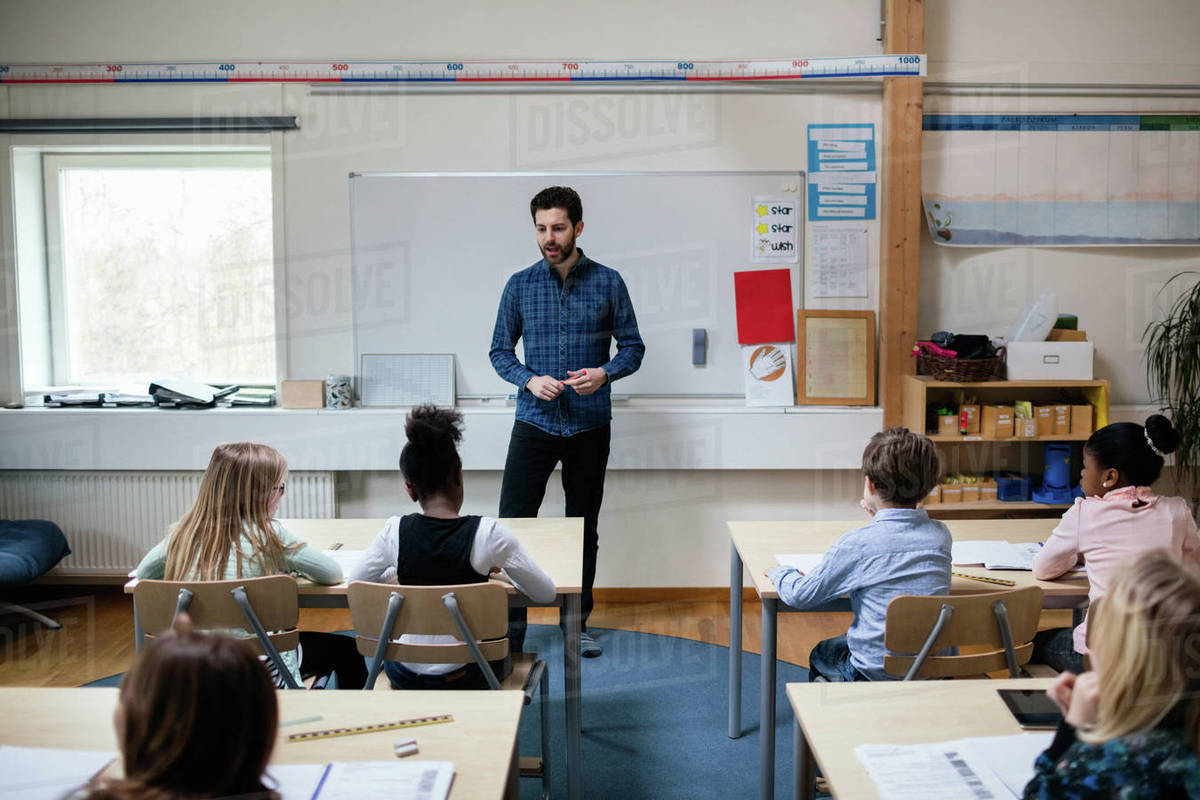 Confident teacher explaining students in classroom at school - Royalty-free Stock Photo | Dissolve