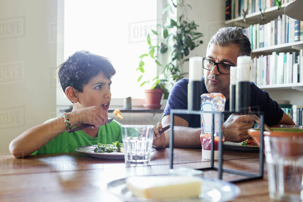 Father and son eating food while sitting at dining table - Stock Photo ...