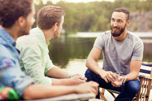 Smiling friends talking while having drink at lakeshore - Royalty-free ...
