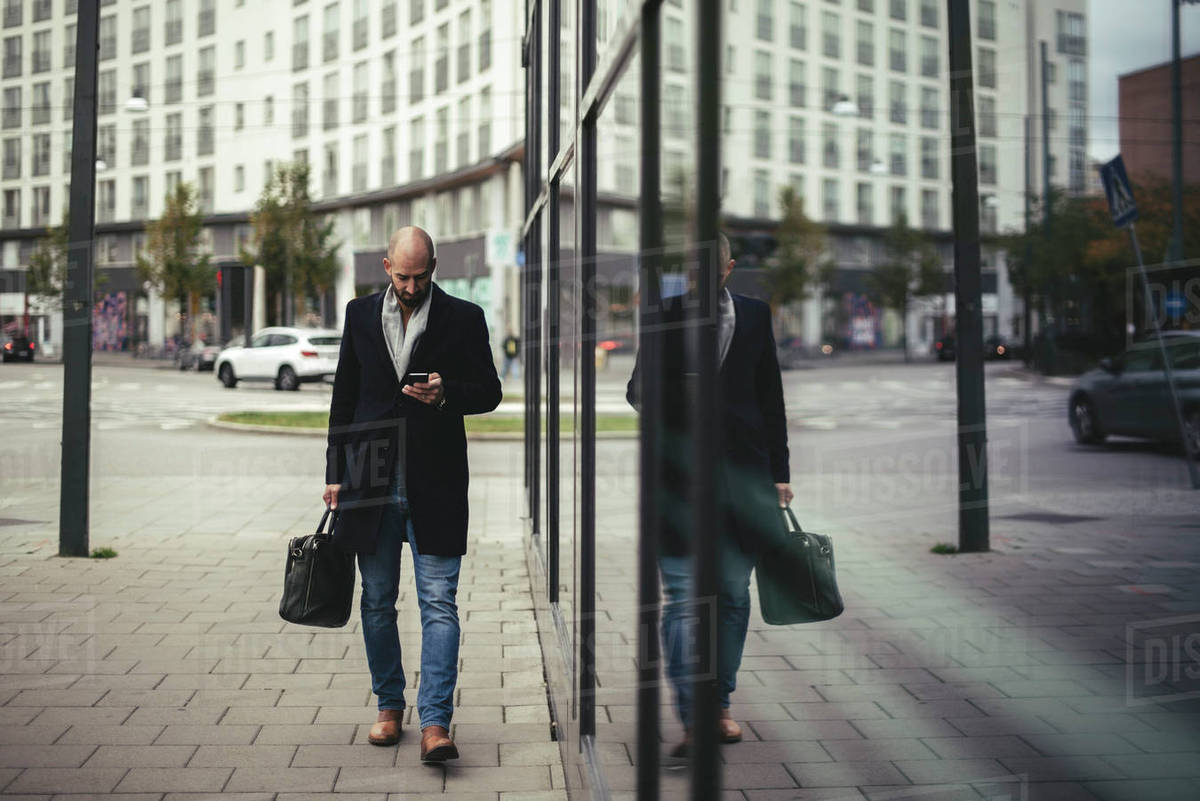 Full length of businessman using mobile phone while walking on sidewalk ...