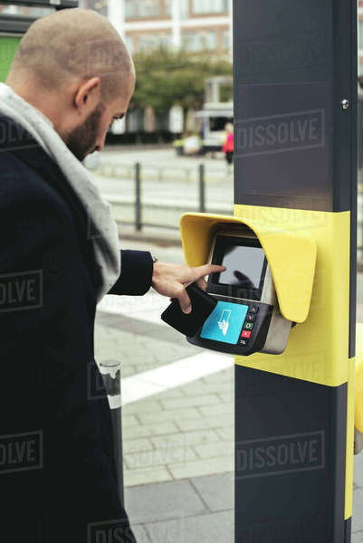 Side view of businessman operating ticket scanner on sidewalk in city ...