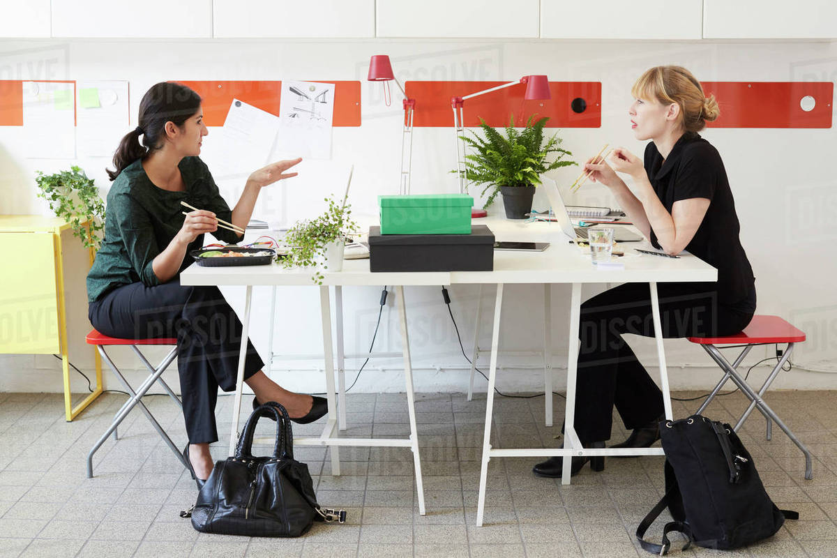 Full length of businesswomen talking while having lunch at table in ...