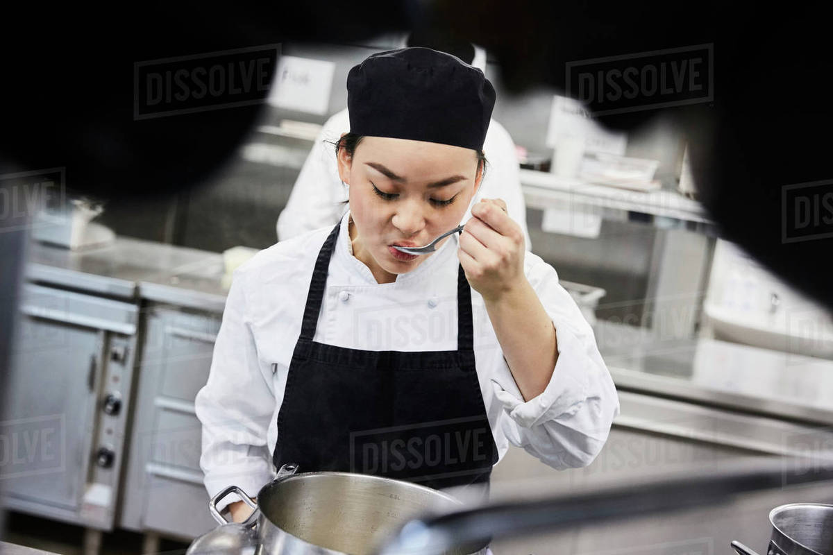 Female chef tasting food from cooking pan at commercial kitchen - Stock ...