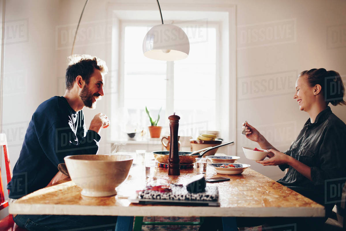 Side view of happy couple talking while eating lunch at home - Royalty ...