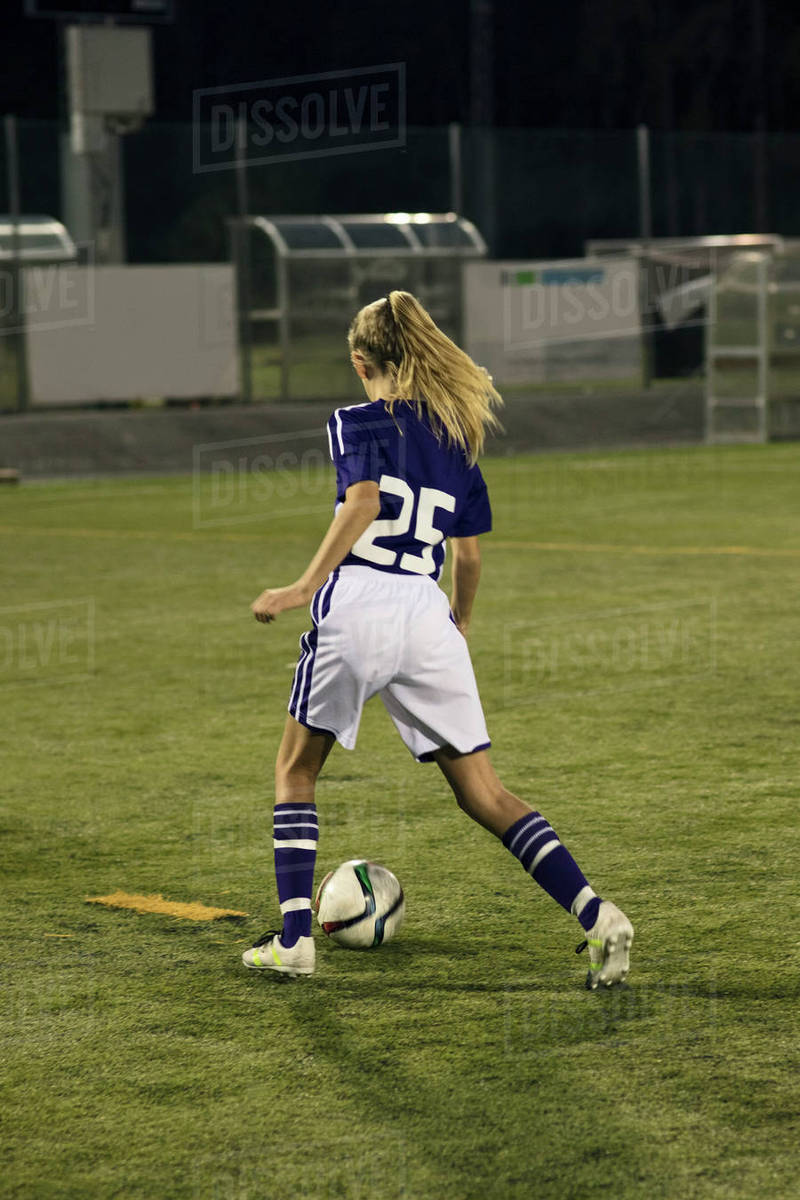 Rear view of girl playing soccer on field at night - Royalty-free Stock ...