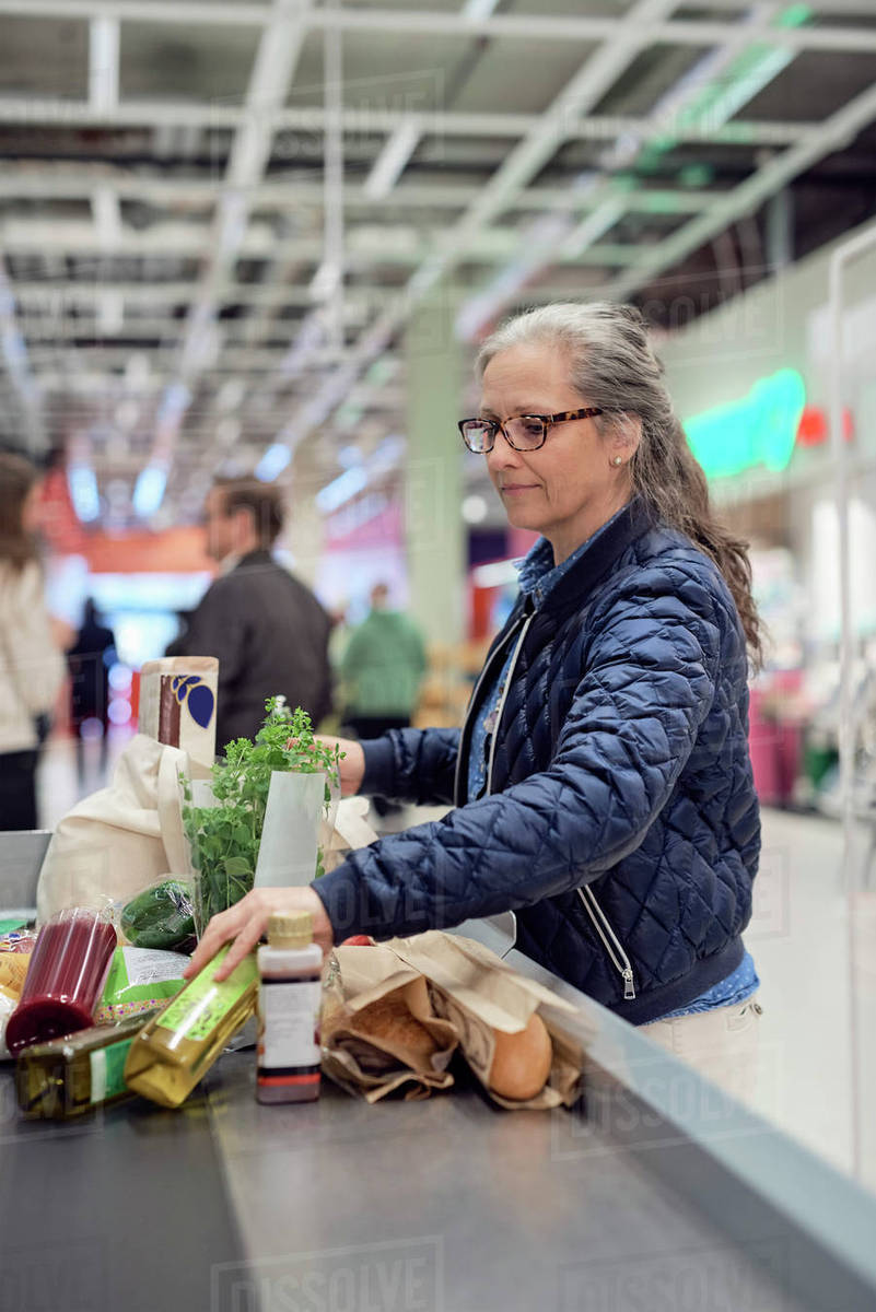 Mature woman standing with groceries and bag at checkout counter in ...