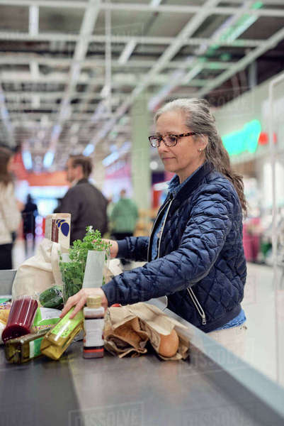 Mature woman standing with groceries and bag at checkout counter in ...